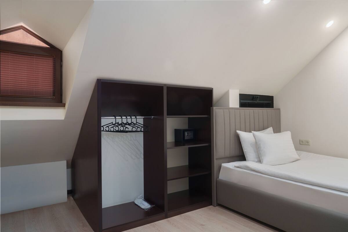 Quarto compacto com cama, guarda-roupa, aquecedor embutido e janela com persianas.