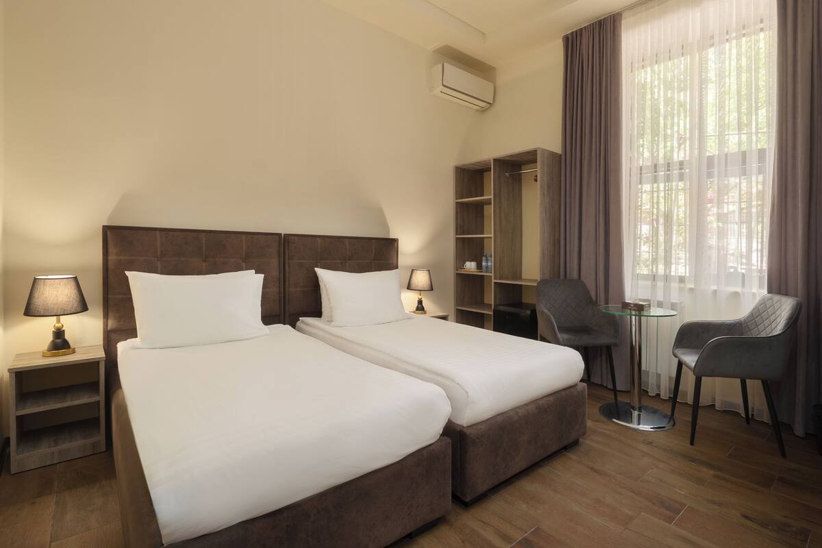 Quarto de hotel com duas camas, uma escrivaninha, uma cadeira e um guarda-roupa.
