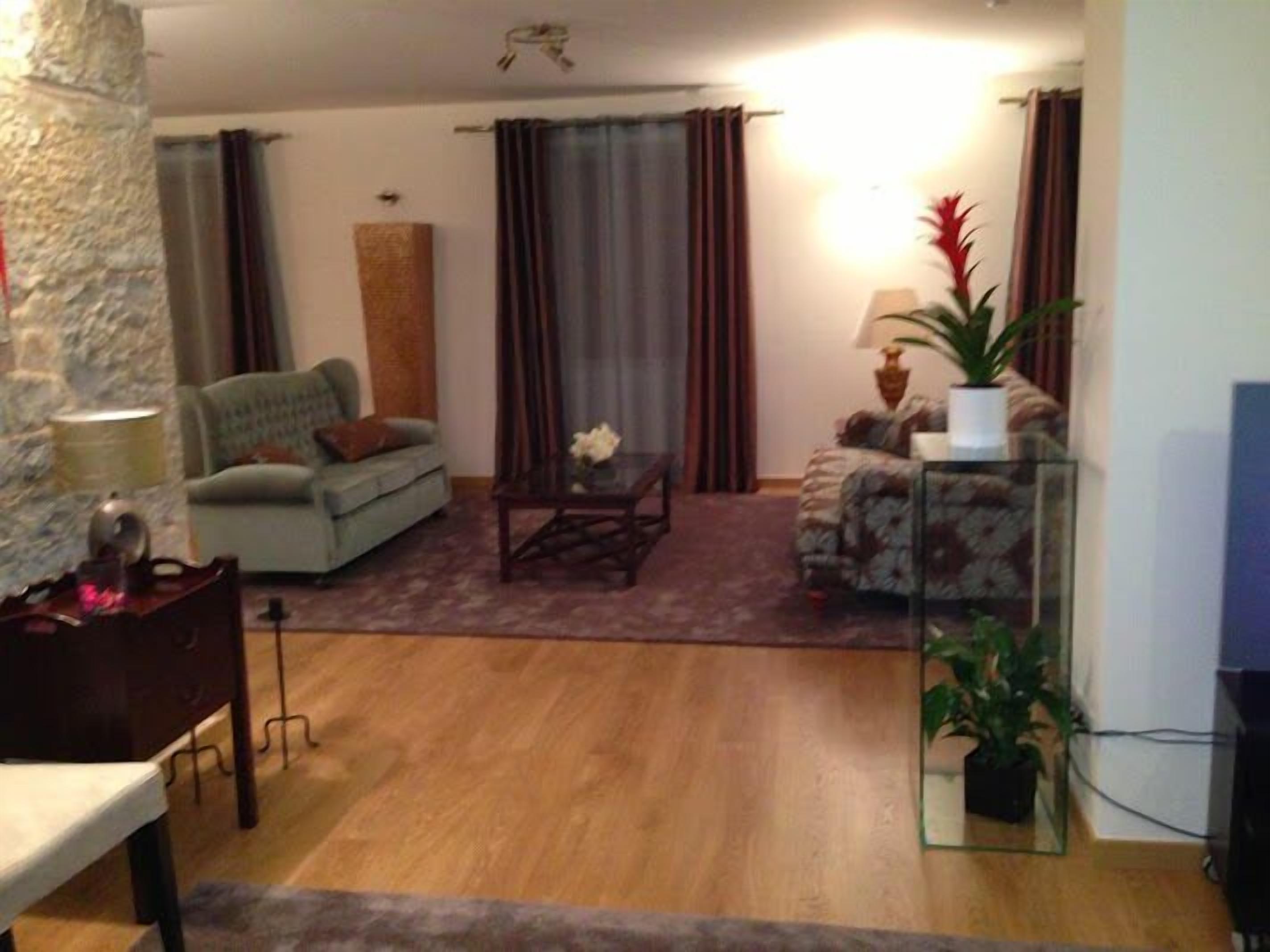 Uma sala de estar com sofá, mesa de centro, poltrona, abajur e aparador com uma planta.
