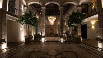Um hall imponente com um lustre central, colunas em arco e piso padronizado.