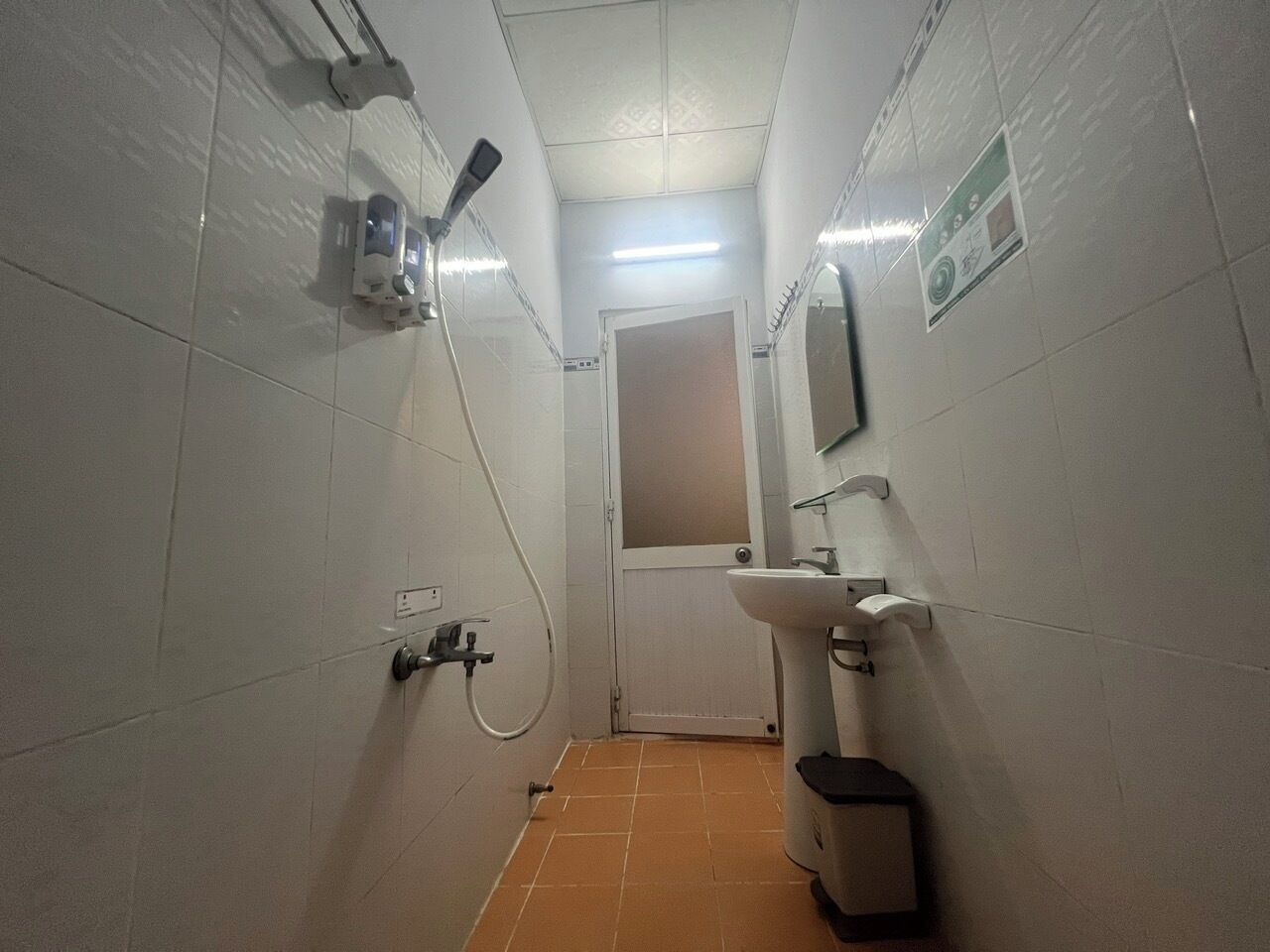 Casa de banho estreita com paredes revestidas a azulejos brancos, uma pia branca e uma porta que dá para outro espaço.
