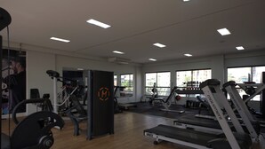 Uma academia com diversos equipamentos de exercício, grandes janelas e piso de madeira.