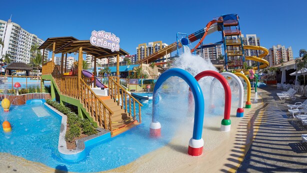 Um parque aquático com um grande tobogã, piscina e área de praia com espreguiçadeiras.