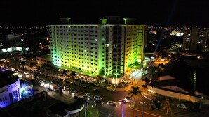 Hotel com vários andares e pátio central, rodeado por um estacionamento e uma rua movimentada.