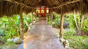 Um caminho serpenteia por um jardim exuberante, com uma construção de telhado de palha.