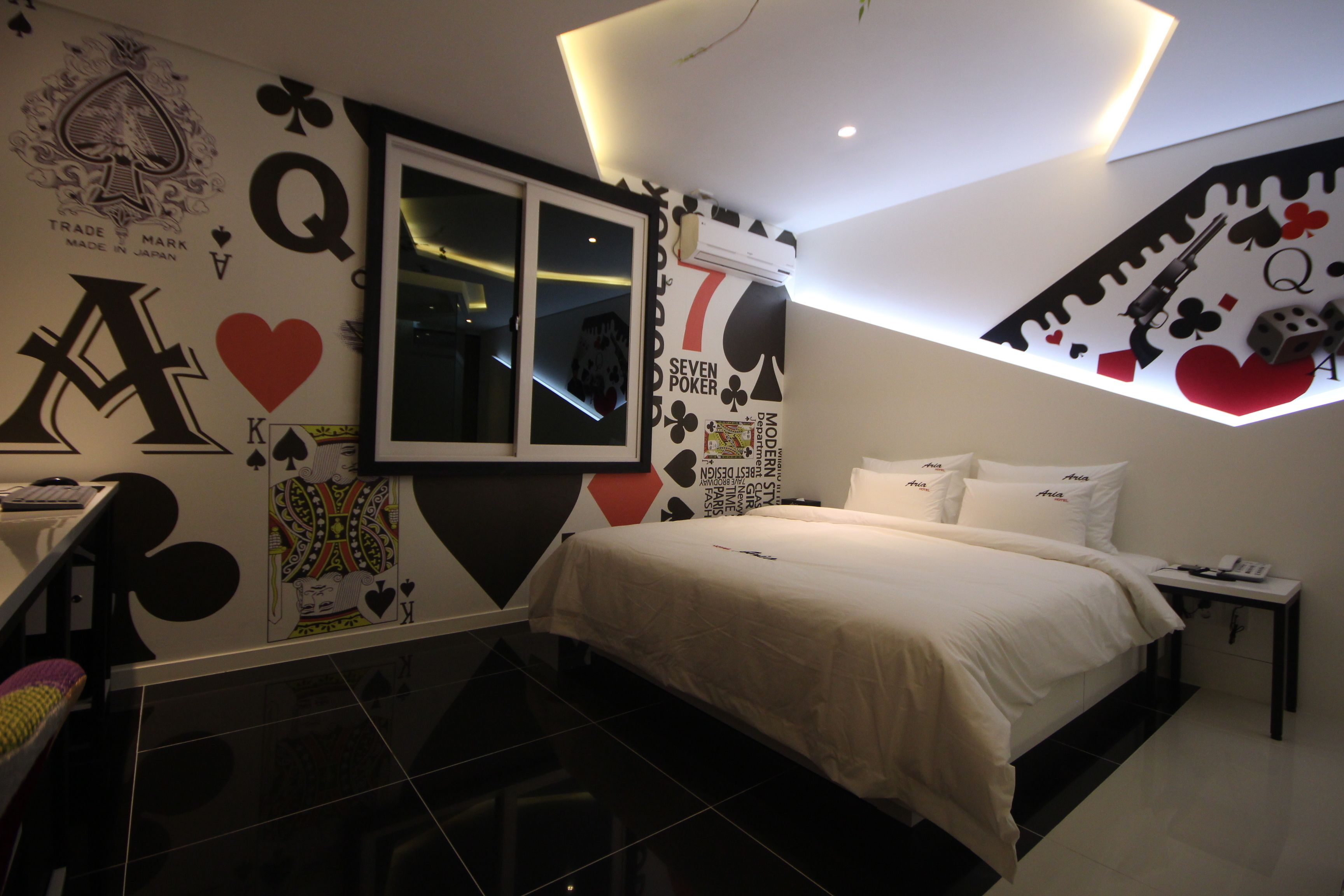 Quarto com cama, mesa de cabeceira e parede decorada com desenhos de cartas de baralho.