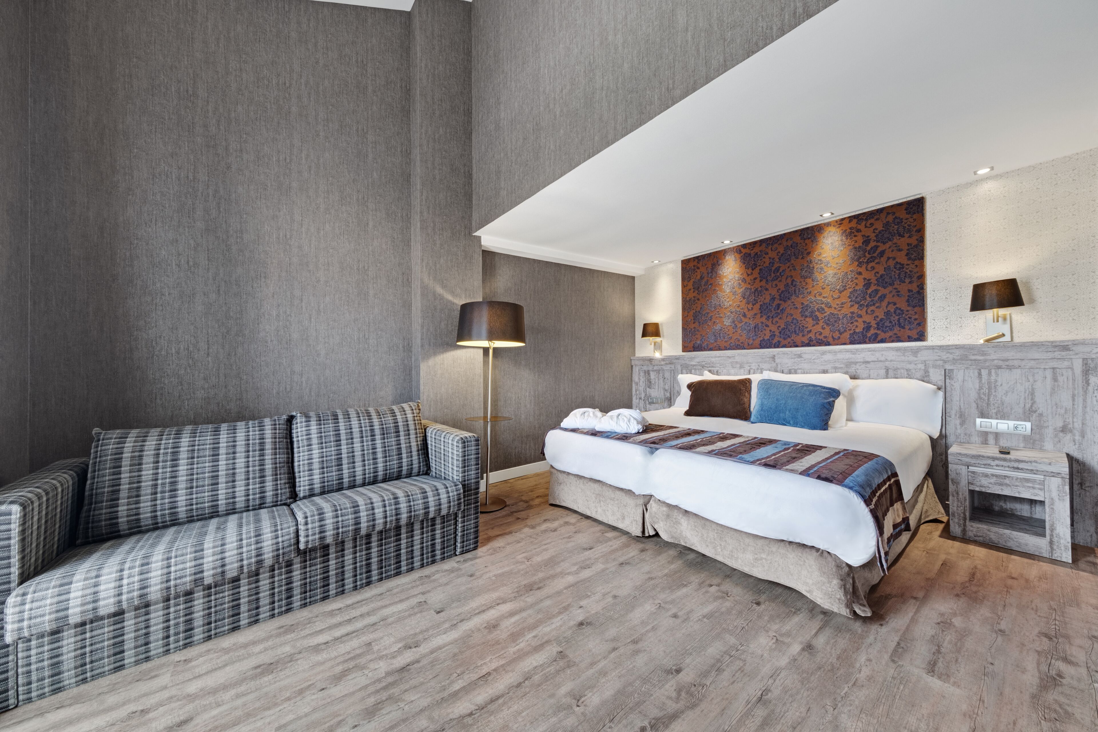 Quarto de hotel moderno com uma cama grande, um sofá e uma mesa de cabeceira.