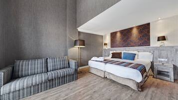 Quarto de hotel moderno com uma cama grande, um sofá e uma mesa de cabeceira.