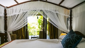 Uma cama com dossel, uma mesa de cabeceira, uma cadeira e vista para o verde lá fora.