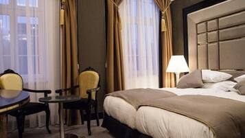 Quarto de hotel com uma cama grande, uma mesinha, duas cadeiras e um abajur.