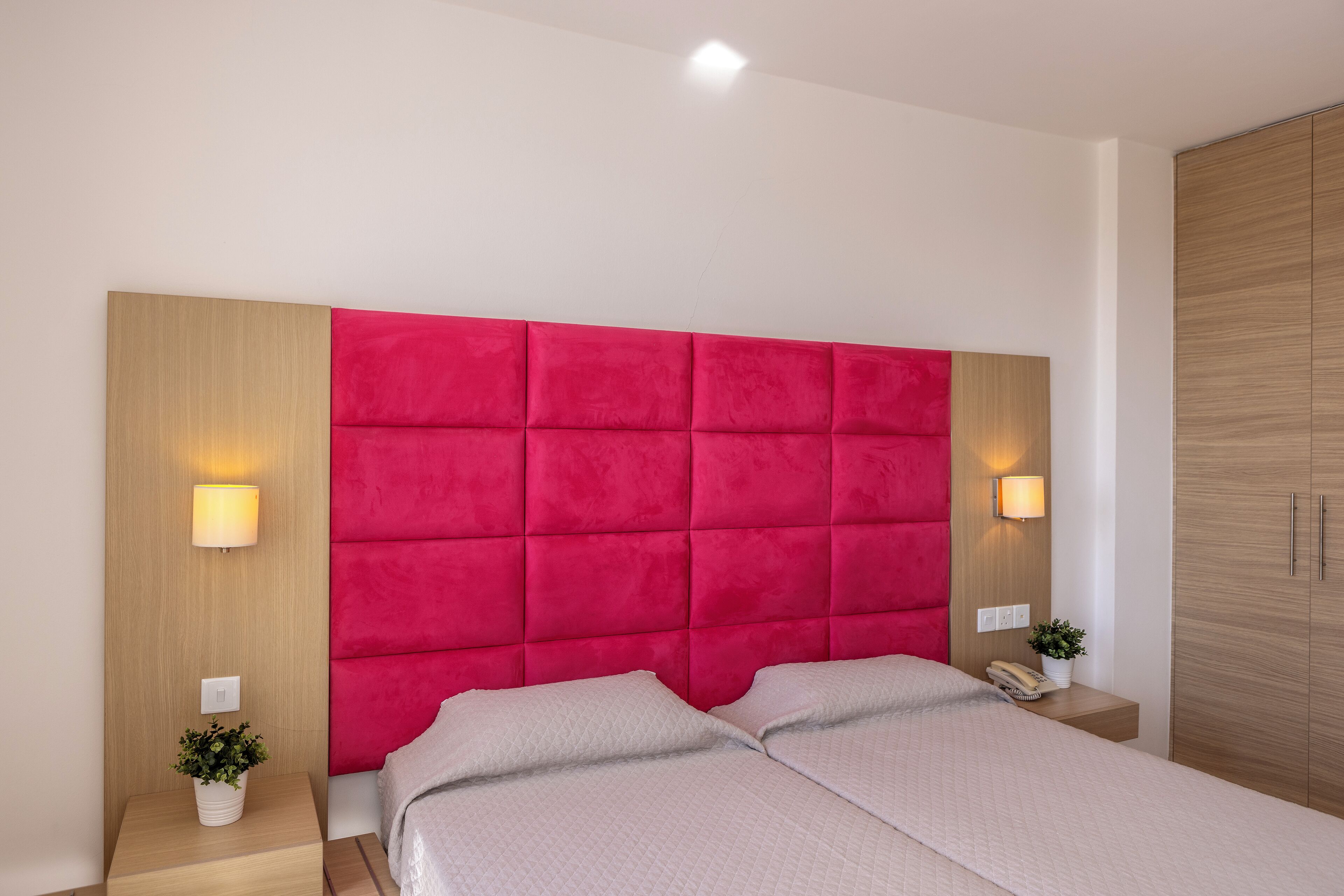 Quarto moderno com uma cama grande, duas mesas de cabeceira com abajures, um guarda-roupa de madeira e uma cabeceira vermelha vibrante.