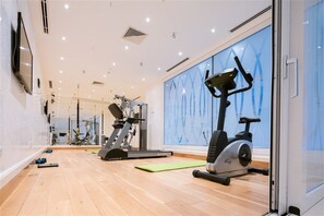 Academia moderna com equipamentos de cardio, um espelho grande na parede e piso de madeira.