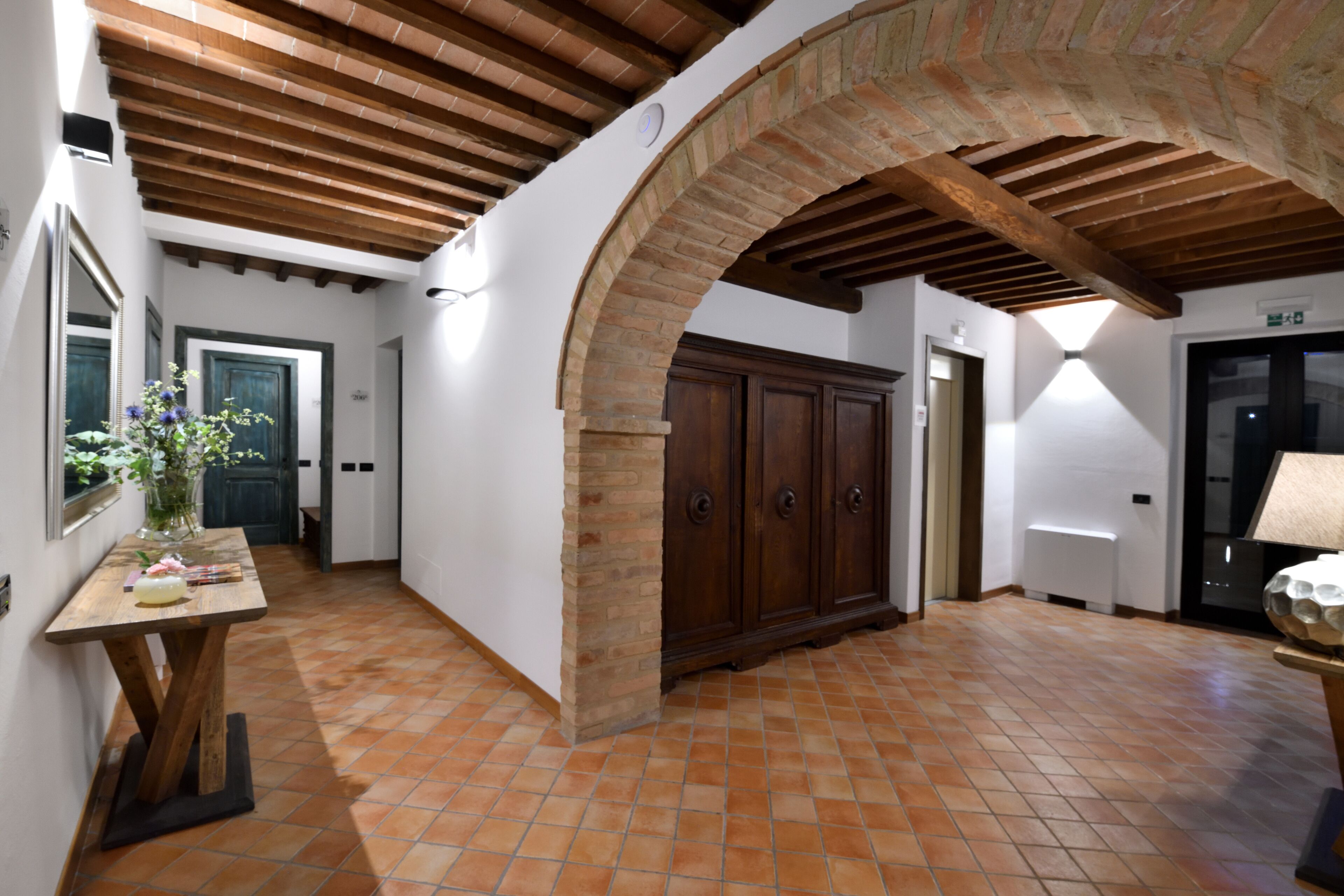Um corredor com piso de azulejos, vigas de madeira, arco de tijolos e um armário de madeira.