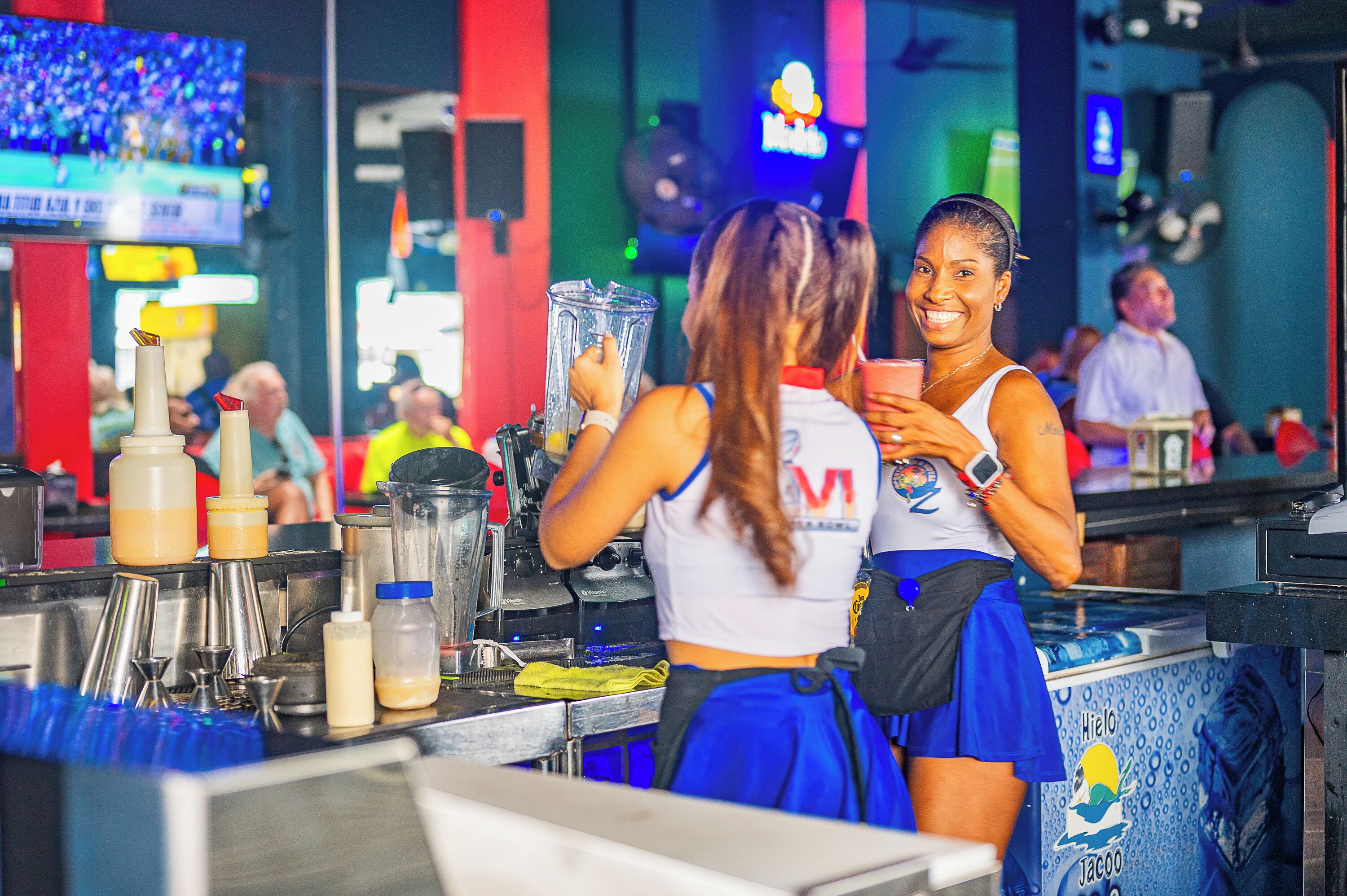 Uma área de bar com balcão, diversos frascos e um liquidificador.