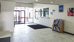 Um lobby limpo e bem iluminado, com balcão de recepção, entrada com porta de vidro, janela e uma estante de livros.