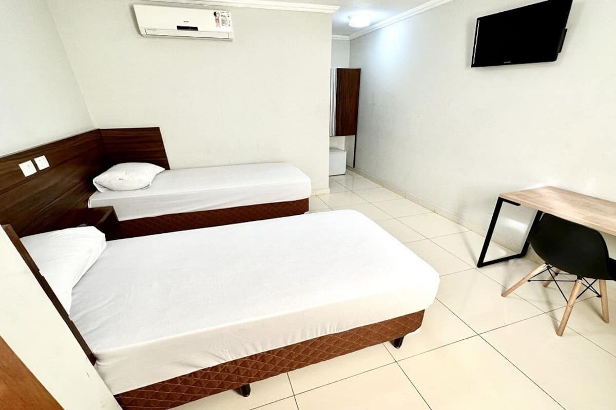 Quarto de hotel com duas camas de solteiro, uma escrivaninha com cadeira, televisão de tela plana e ar condicionado.