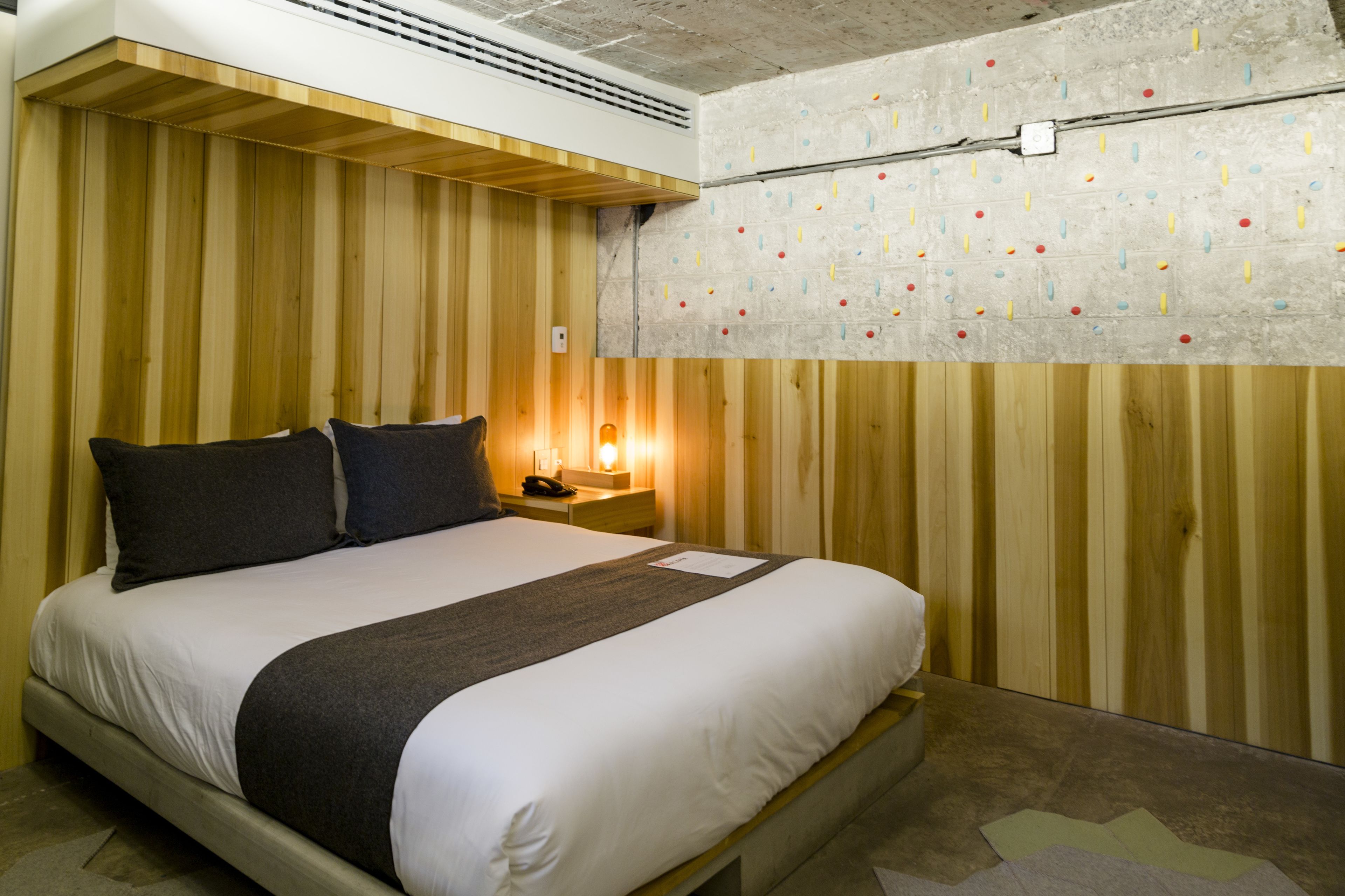 Quarto de hotel com cama, paredes de painel de madeira, parede de escalada fixada e mesa de cabeceira com lumin ária.