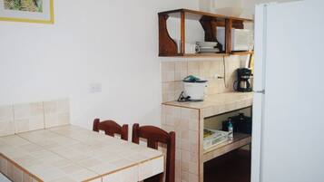 Uma cozinha com painel de azulejos, uma mesa de madeira e cadeiras. Há uma cafeteira e uma torradeira no balcão.