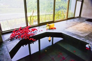 Quarto com uma janela grande, um pequeno elemento aquático no interior e vista para o verde lá fora.