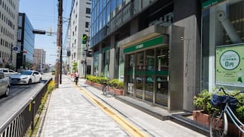 Rua urbana com um edifício exibindo uma placa verde de um banco e uma bicicleta estacionada na frente.