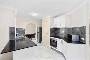 Uma cozinha moderna com armários brancos, bancada preta, forno embutido e micro-ondas.