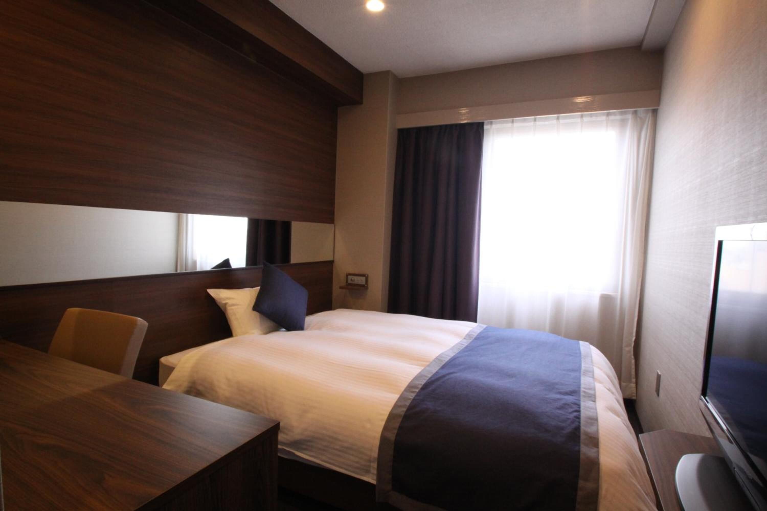 Quarto de hotel com uma cama grande, escrivaninha, cadeira e televisão.