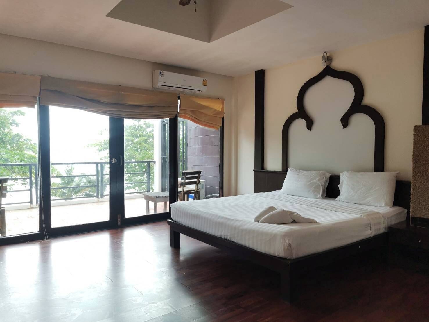 Quarto com cama grande, ar condicionado, varanda com mesa e cadeiras e vista para o verde lá fora.