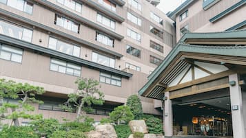 Um hotel com vários andares, entrada coberta e um jardim com pedras e árvores.