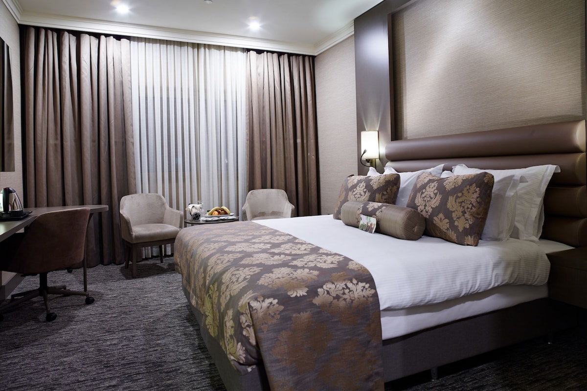Quarto de hotel com uma cama grande, duas poltronas, uma escrivaninha e uma mesa de jantar.