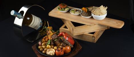 Uma mesa de madeira com uma garrafa de vinho, uma saladeira e um prato de legumes grelhados.