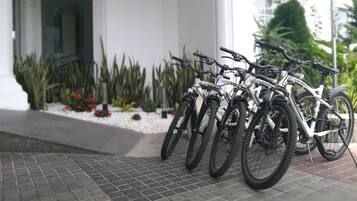 Uma fileira de bicicletas estacionadas em frente a um edifício com entrada em azulejos e um jardim com plantas e flores.