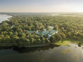 Vista aérea de um resort amplo e isolado, com vários edifícios cercados por floresta densa e corpos d'água.