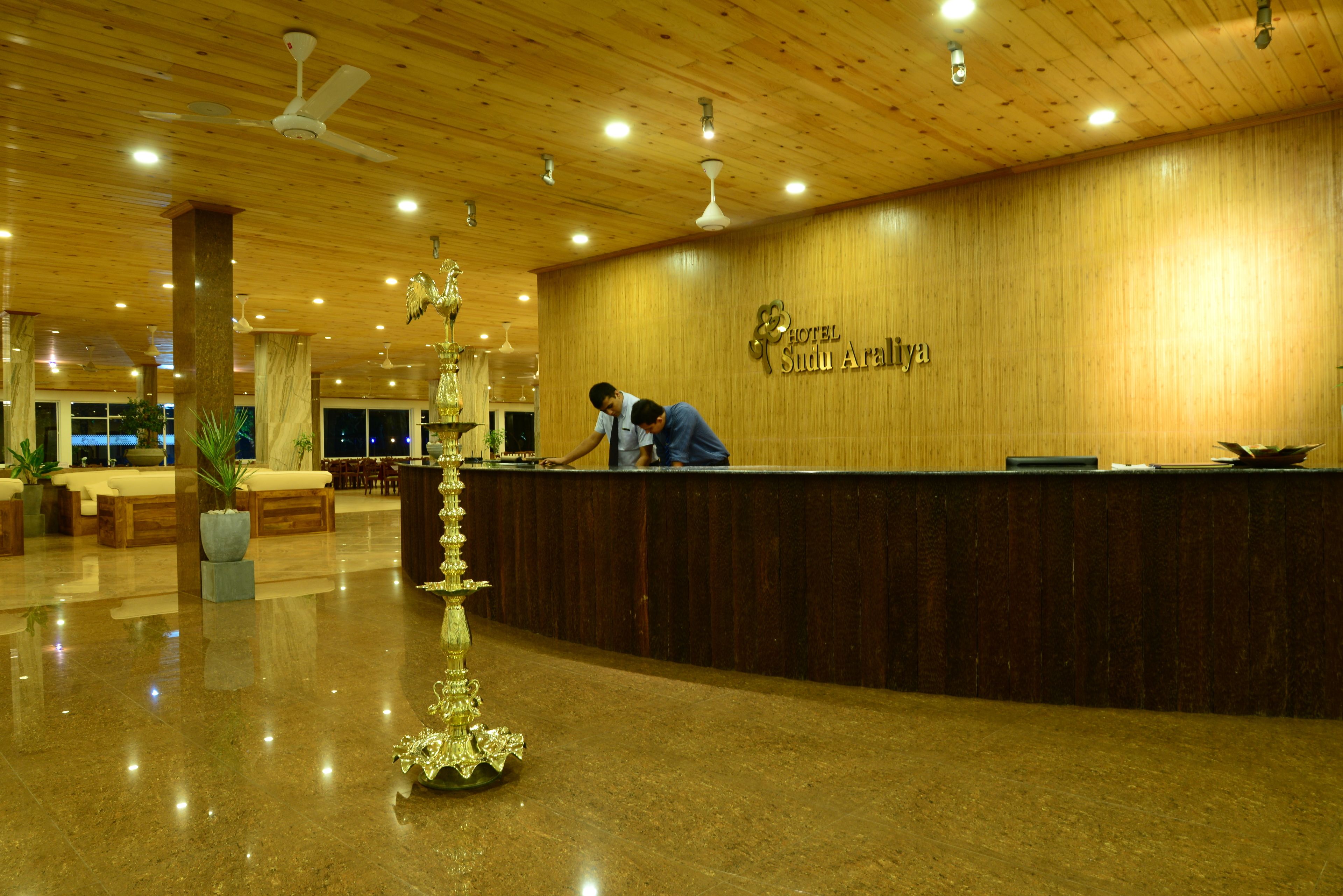 Um hall de hotel com uma recepção de madeira, um recepcionista e uma fonte decorativa.