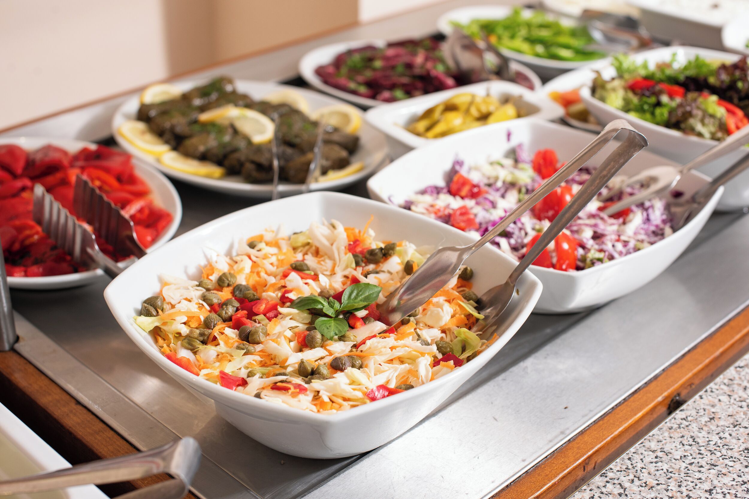 Uma mesa de buffet com diversos pratos, incluindo saladas, legumes e uma tigela de salada de repolho.
