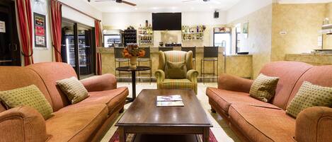 Uma sala de estar com dois sofás, uma mesa de centro, uma televisão e uma área de cozinha ao fundo.