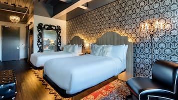 Quarto de hotel moderno com uma cama grande, uma cama menor, um chaise longue e um papel de parede estampado.
