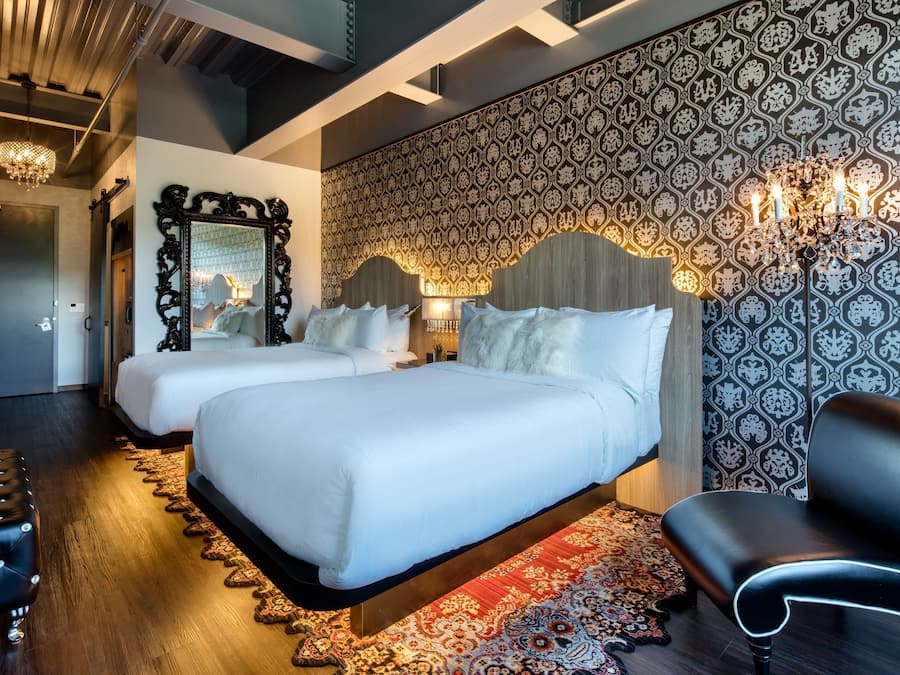 Quarto de hotel moderno com uma cama grande, uma cama menor, um chaise longue e um papel de parede estampado.