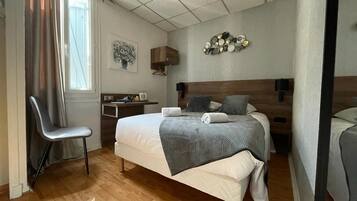 Quarto com cama, cadeira, mesa de cabeceira e um objeto decorativo na parede.