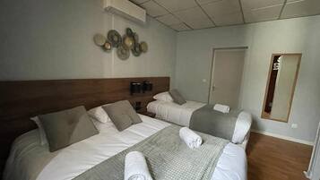 Quarto de hotel com duas camas, cabeceira de madeira, ar condicionado fixado na parede e um espelho.