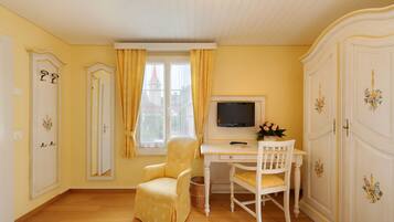 Quarto com piso de madeira, escrivaninha com televisão, cadeira, guarda-roupa e janela com cortinas.