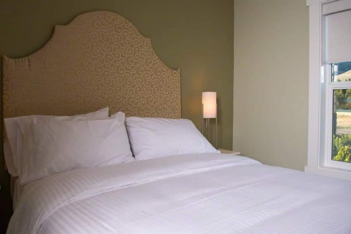 Cama bem arrumada com lençóis brancos em quarto com cabeceira estampada. Há duas luminárias de cabeceira de cada lado da cama.