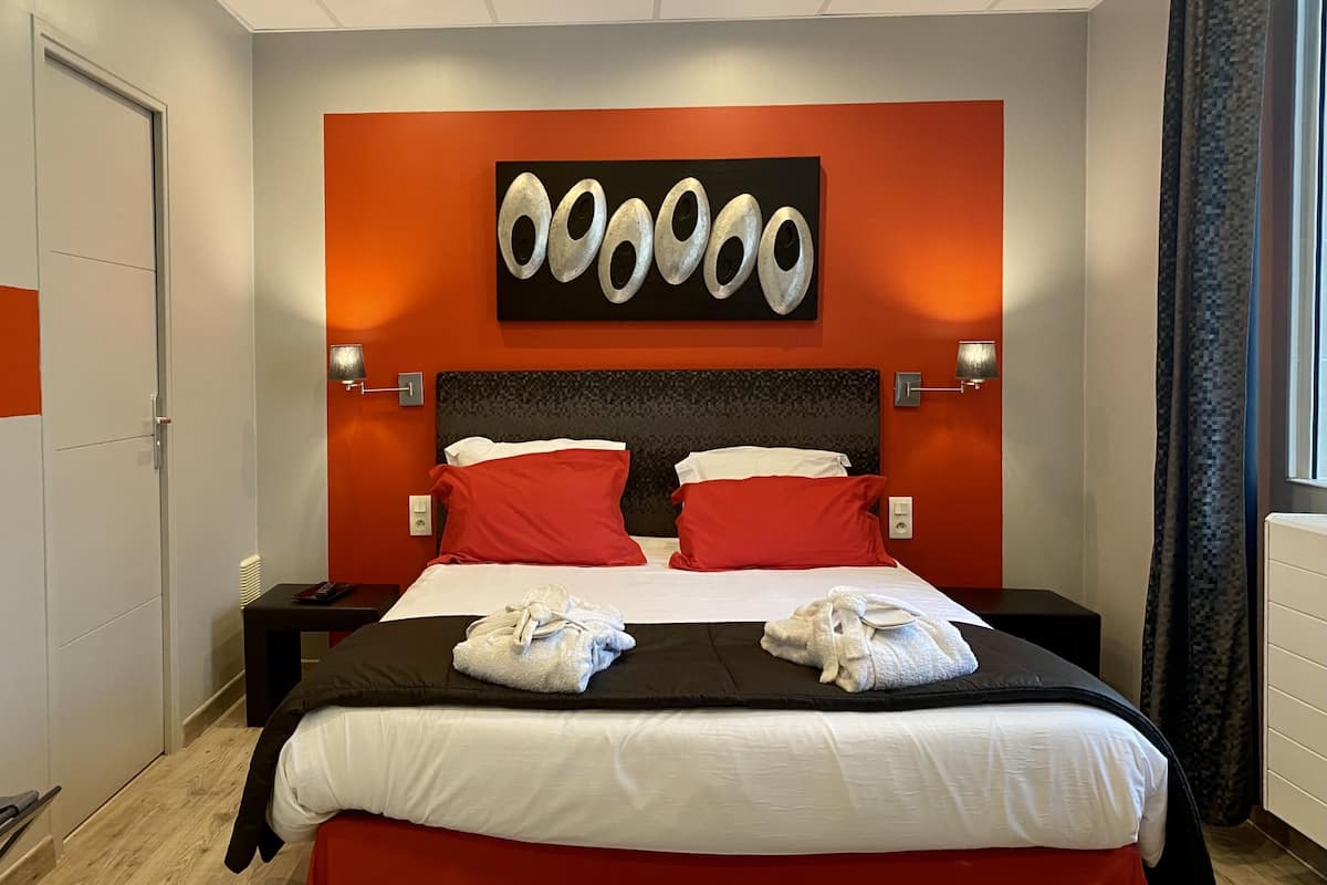 Quarto de hotel moderno com uma cama grande, almofadas vermelhas e brancas e uma peça de arte original na parede.