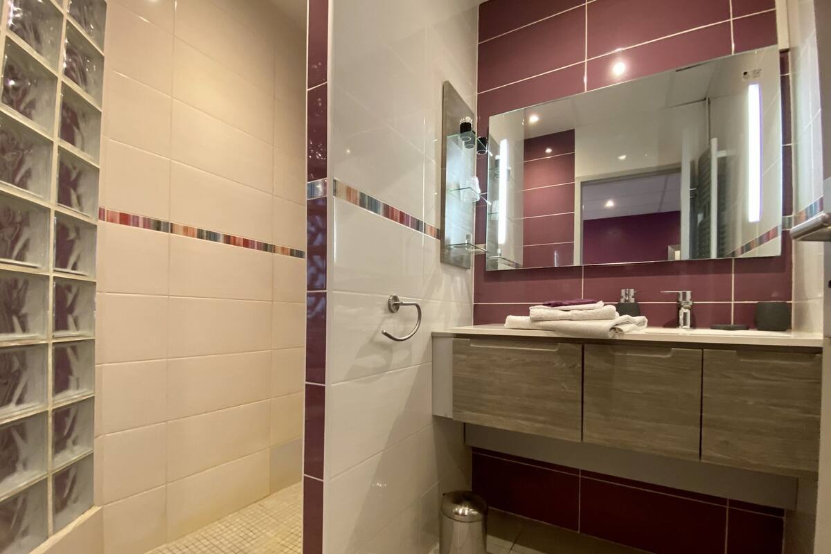 Uma casa de banho moderna com cabine de duche em vidro, toucador com espelho e um contentor de lixo.