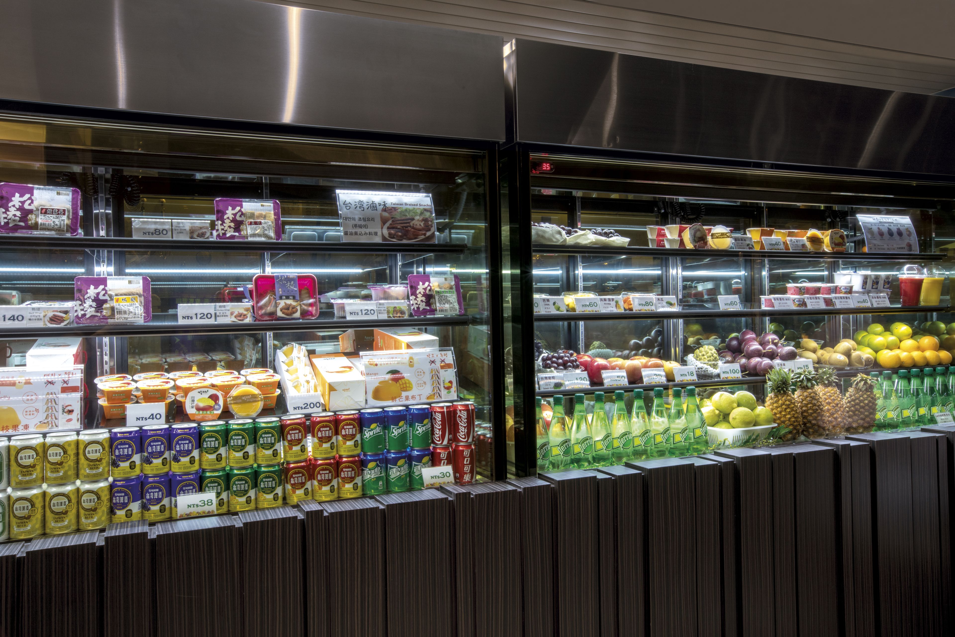 Vitrine refrigerada com diversos alimentos e bebidas, incluindo snacks embalados, bebidas e produtos frescos.