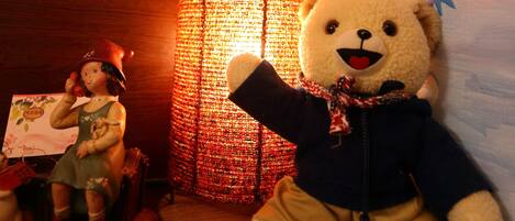 Um urso de pelúcia e uma figurina sobre uma superfície de madeira, com uma luminária vermelha texturizada ao fundo.