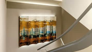 Uma escadaria com design moderno, uma obra de arte na parede retratando uma paisagem e um teto com claraboia.