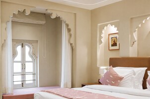 Quarto com cama, mesa de cabeceira, janela com cortinas e porta com molduras decorativas.