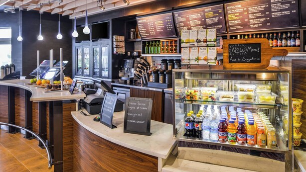 Interior moderno de café com balcão, quadros de menu e vitrine com bebidas.