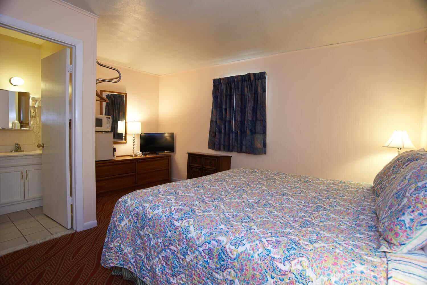 Quarto de hotel com cama, televisão, cômoda e banheiro visível por uma porta aberta.