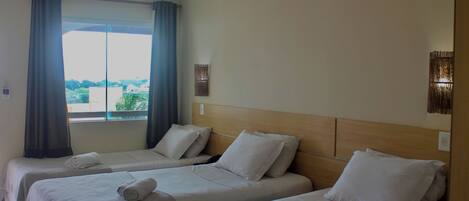 Quarto de hotel com duas camas, uma janela grande com cortinas e vista para o verde lá fora.